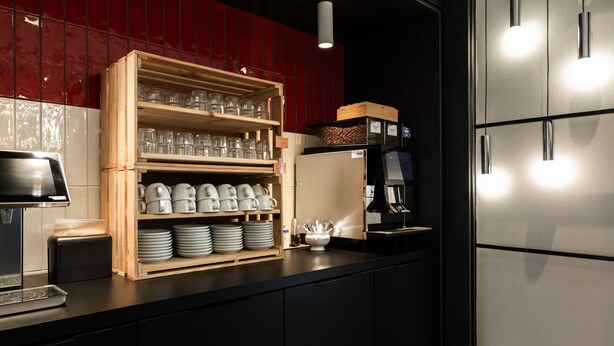 Uma cozinha moderna com prateleiras de madeira que exibem copos e pratos, uma máquina de café e uma geladeira de aço inoxidável.
