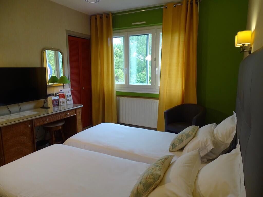 Quarto de hotel com duas camas, uma escrivaninha com televisão, uma cadeira e uma janela com cortinas.
