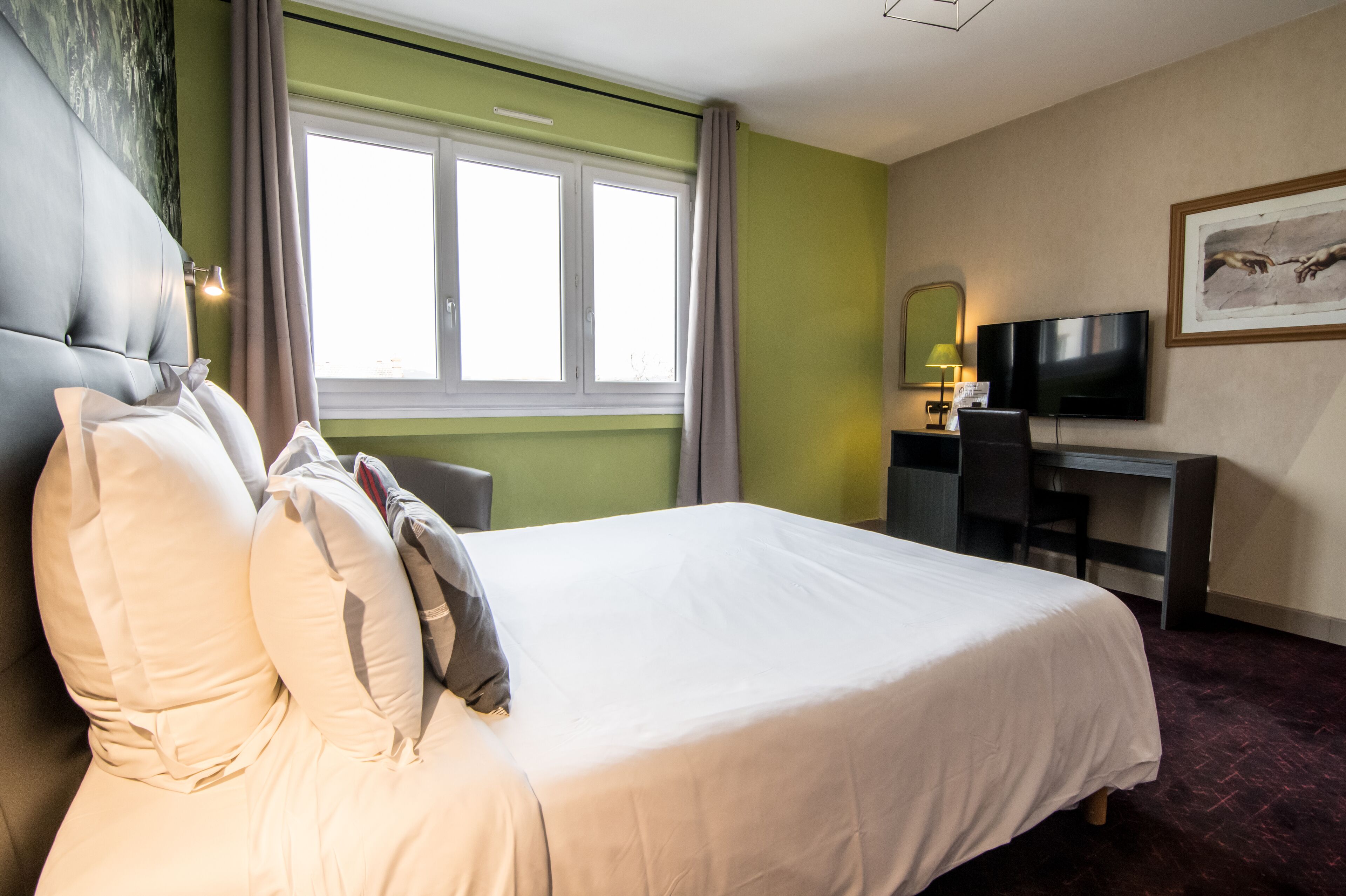 Quarto de hotel com uma cama grande, uma escrivaninha, uma televisão e uma janela com cortinas.