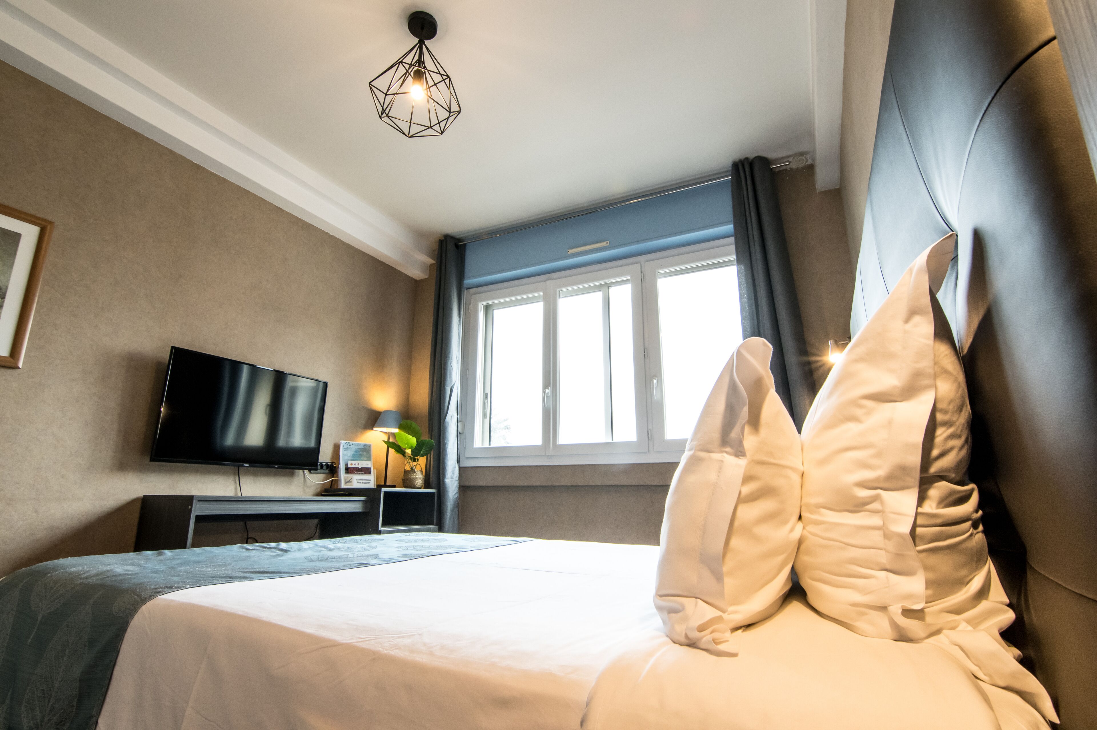 Quarto de hotel com cama, televisão de tela plana, escrivaninha e janela com cortinas.