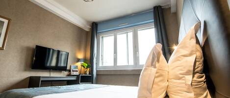 Quarto de hotel com cama, televisão de tela plana, escrivaninha e janela com cortinas.