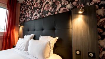 Quarto de hotel com cabeceira estofada, roupa de cama branca e papel de parede com motivos florais.