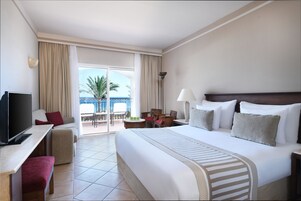 Quarto de hotel com cama, mesa de trabalho com televisão, cadeira, mesa e vista para o exterior.