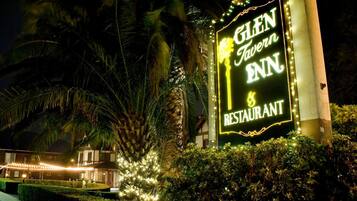 Placa neon do Restaurante Glen Inn, rodeada por palmeiras e sebes bem cuidadas.