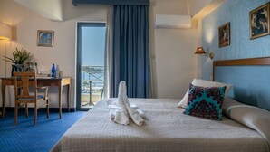 Quarto de hotel com cama, escrivaninha, cadeira, varanda e uma vista, além de um quadro na parede.