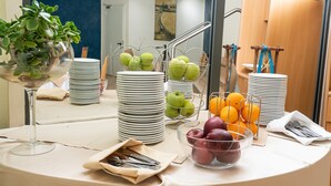 Disposição de buffet com pratos empilhados, tigelas de frutas e uma taça de vinho.