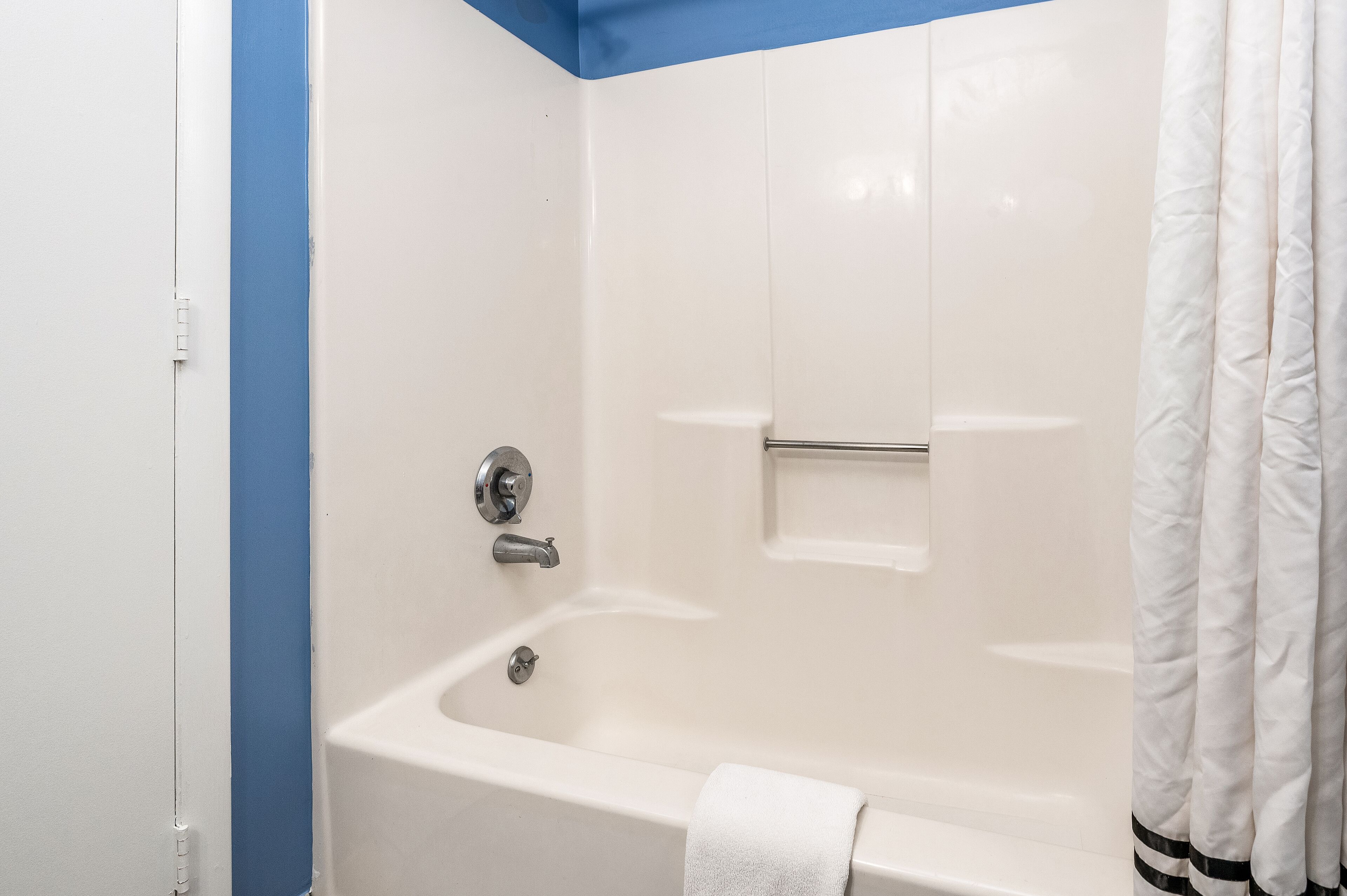 Um banheiro com banheira, toalha, cortina de chuveiro e uma parede azul decorativa.