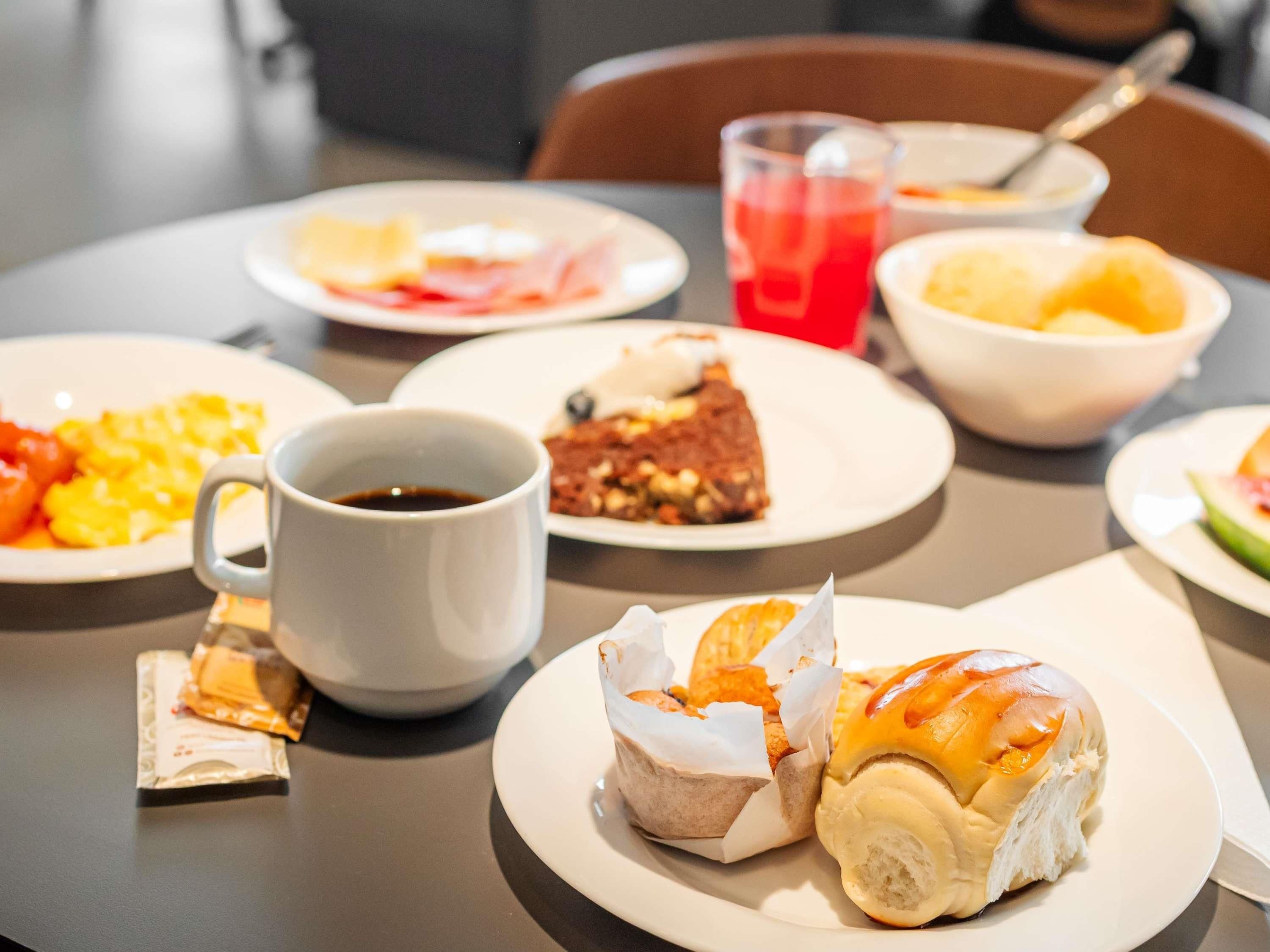 Mesa de café da manhã com pratos de comida, uma caneca e um copo de bebida vermelha.