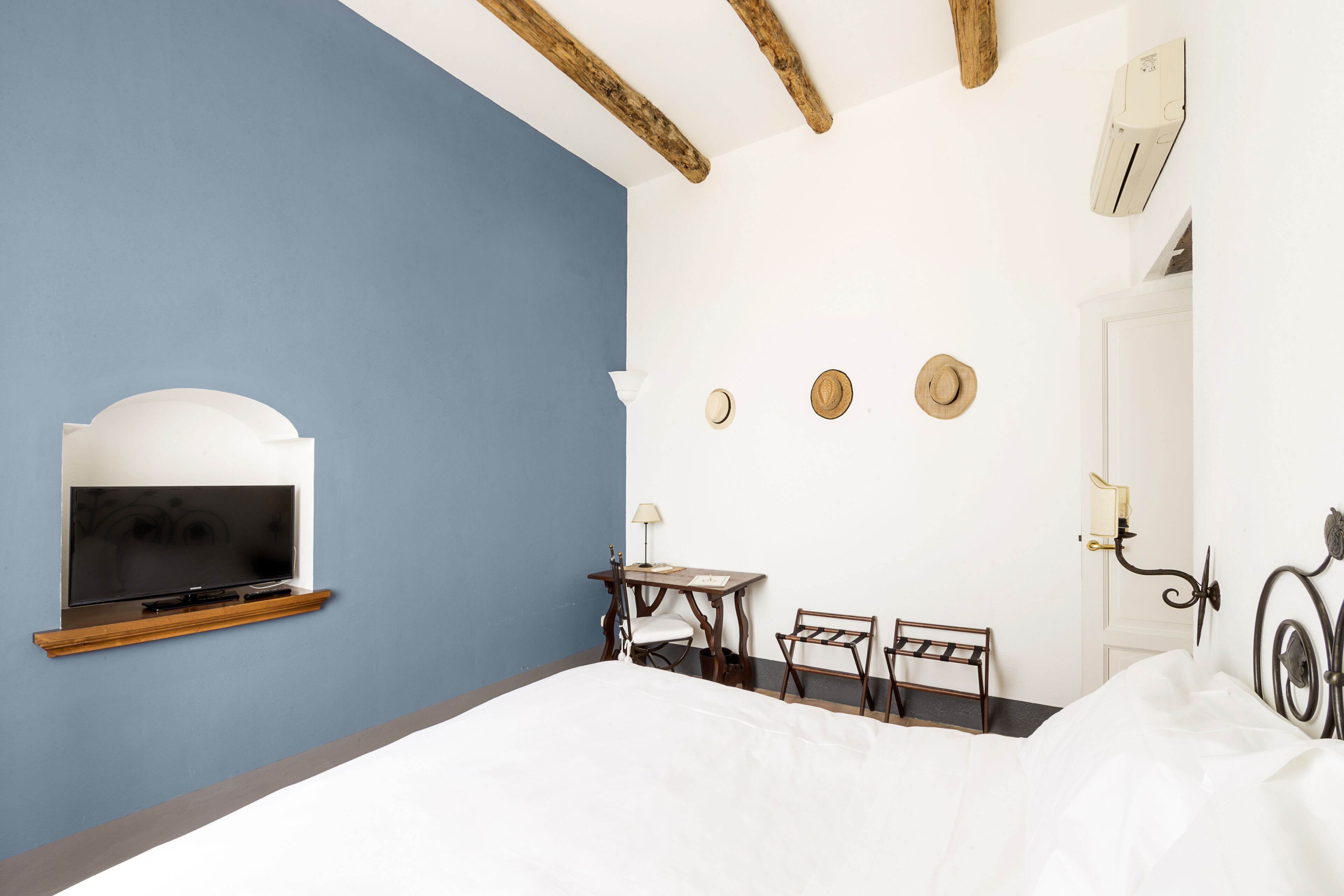 Quarto com cama, escrivaninha, cadeira, televisão e ar condicionado fixado na parede.