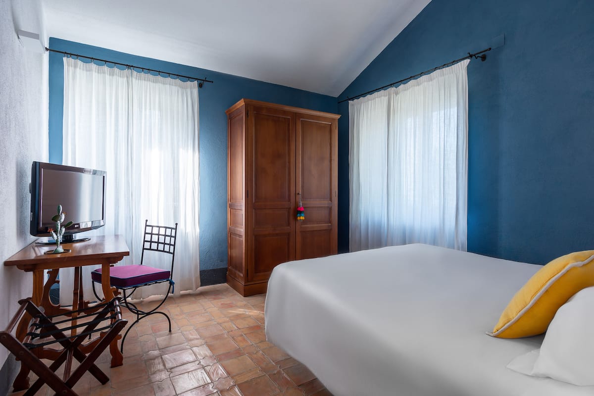 Um quarto com cama, televisão, guarda-roupa de madeira, cadeira e mesa.