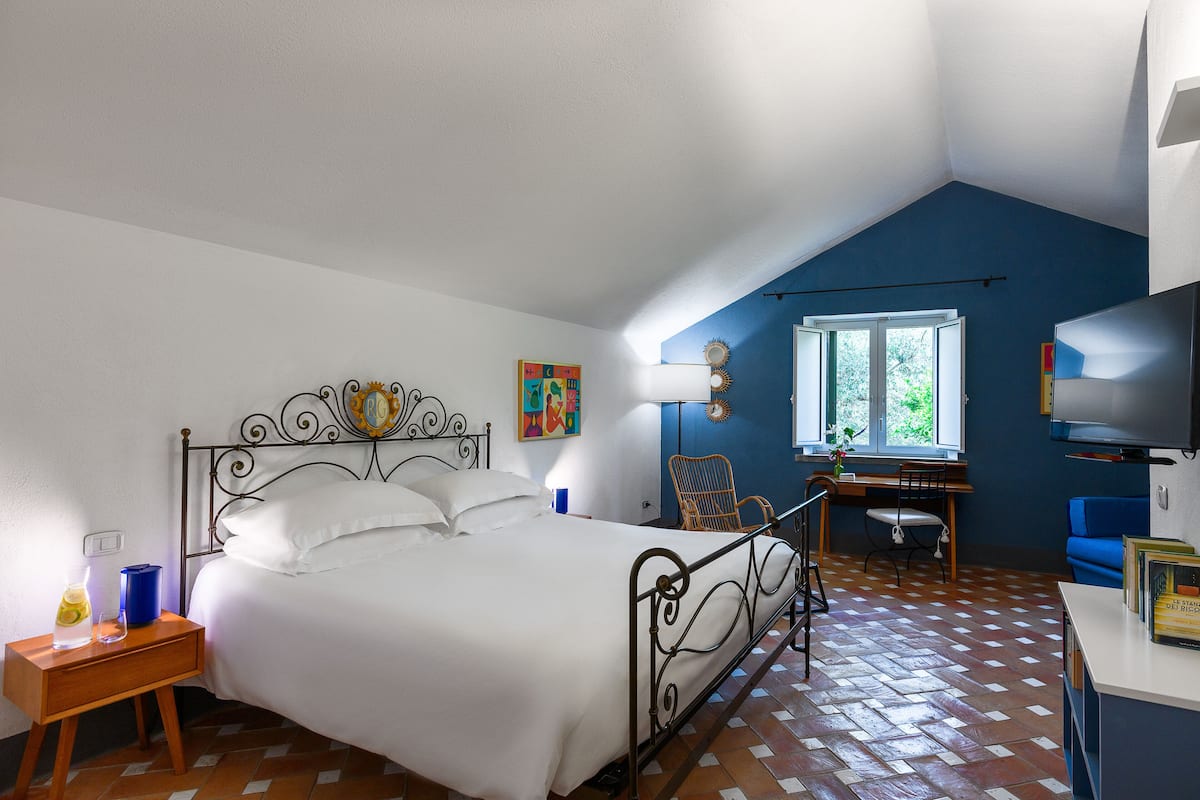 Quarto com cama, escrivaninha, cadeira e televisão.