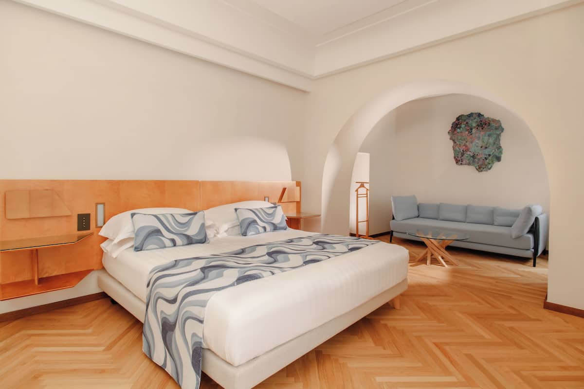 Um quarto moderno com uma cama grande, uma mesinha de cabeceira de madeira, um sofá azul e um objeto decorativo na parede.