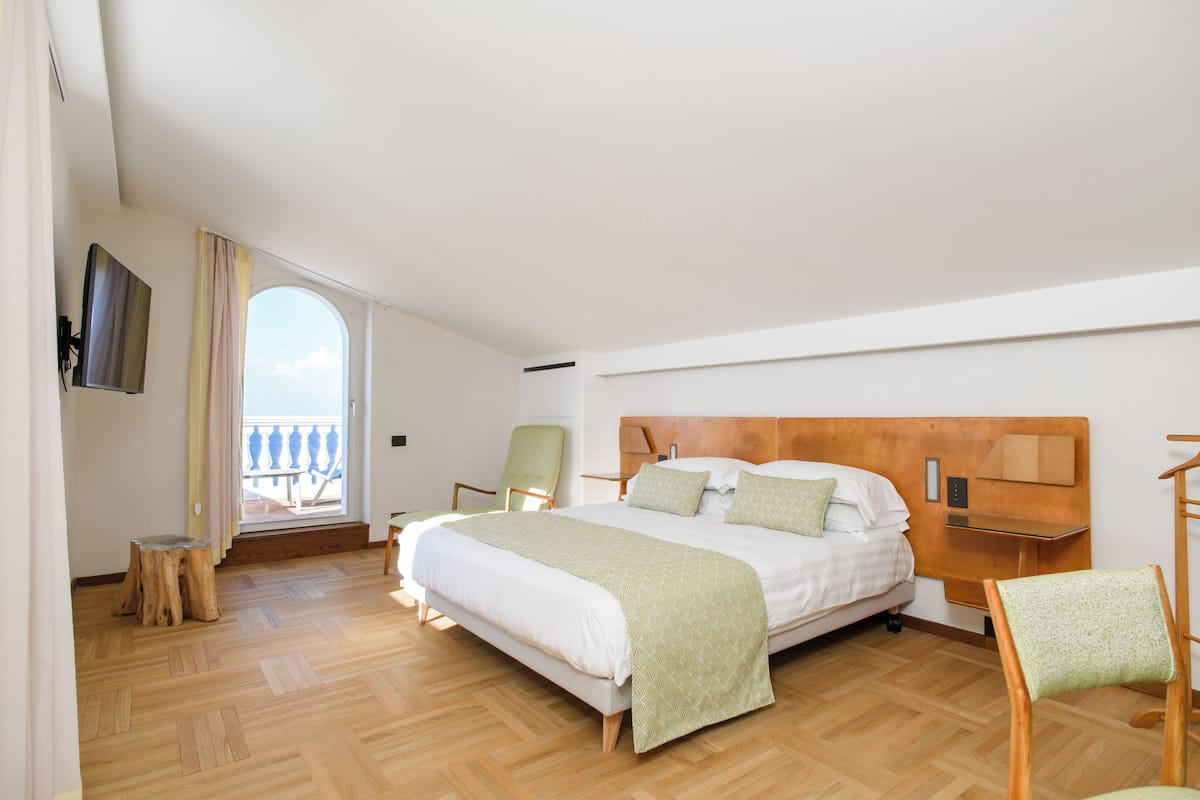 Quarto de hotel com uma cama grande, cabeceira de madeira, televisão fixada na parede e varanda com guarda-corpo.