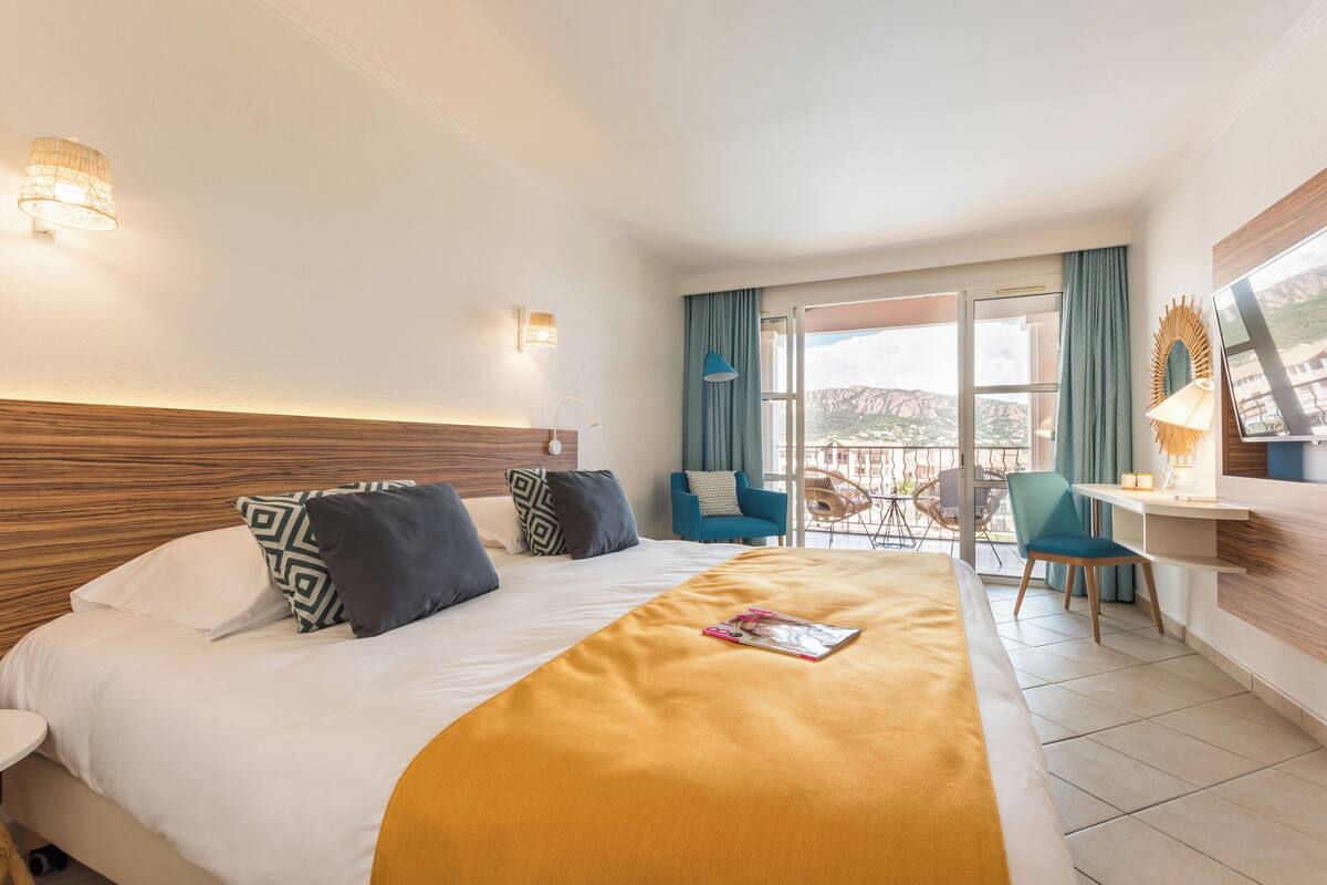 Quarto de hotel com cama, secretária, cadeira e varanda com vista.