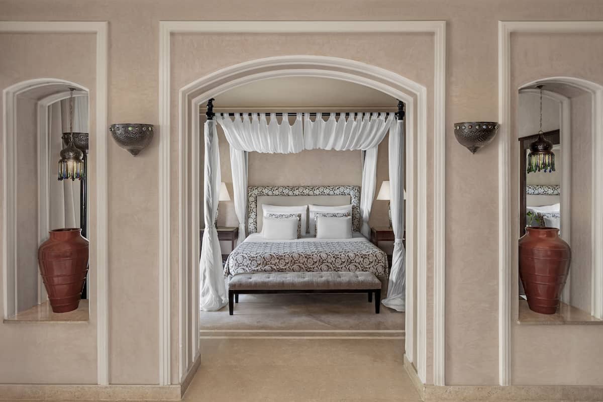 Quarto com cama de dossel, um espelho grande e um vaso na mesa de cabeceira.