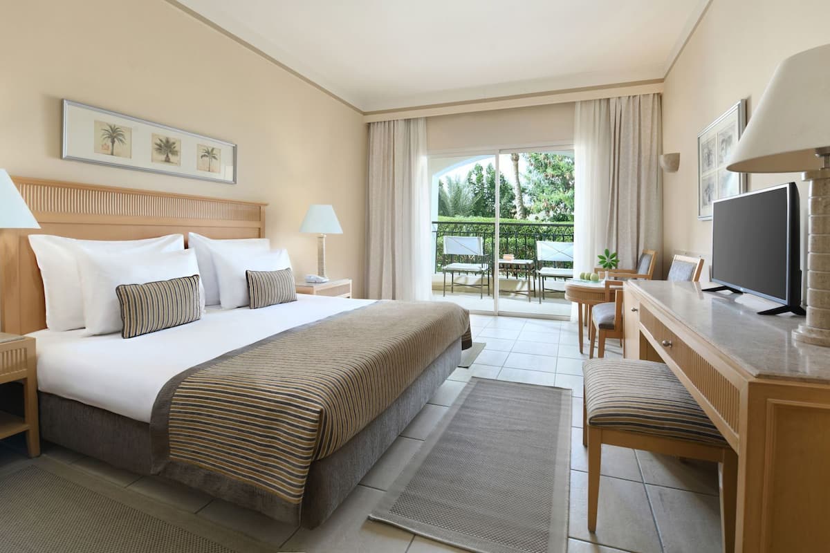Quarto de hotel com cama, mesas de cabeceira, escrivaninha, televisão e varanda com área de estar ao ar livre.
