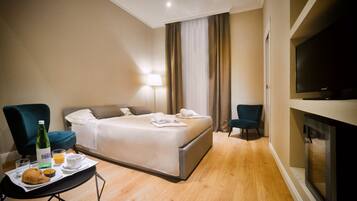 Quarto de hotel com cama, duas poltronas, televisão, mesa com café da manhã e janela com cortinas.