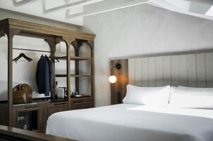 Quarto de hotel com cama, guarda-roupa de madeira, cabideiro e luminária fixada na parede.