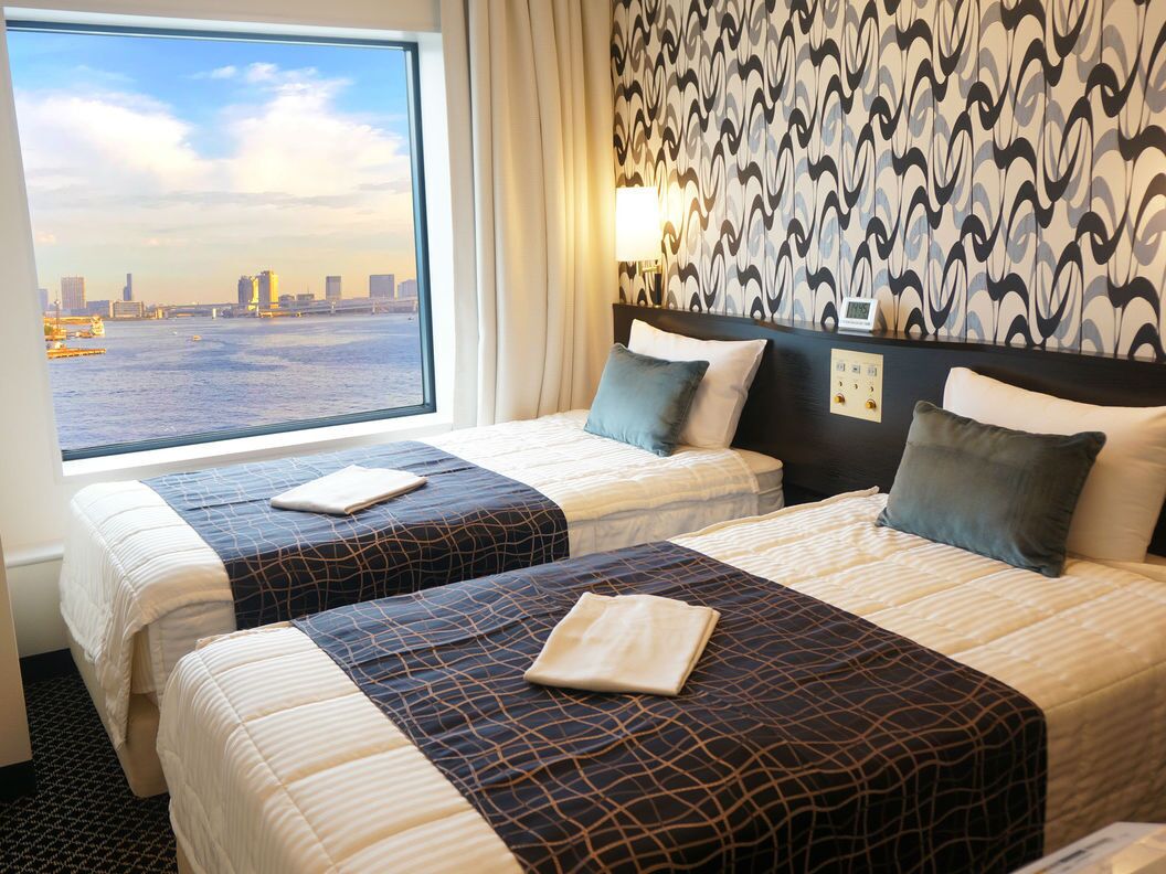 Quarto de hotel com duas camas, vista para o horizonte urbano e parede com padrão.