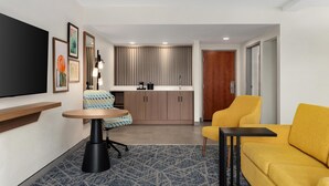 Uma sala moderna com sofá, televisão, mesa pequena e área de cozinha com bancada e armários.