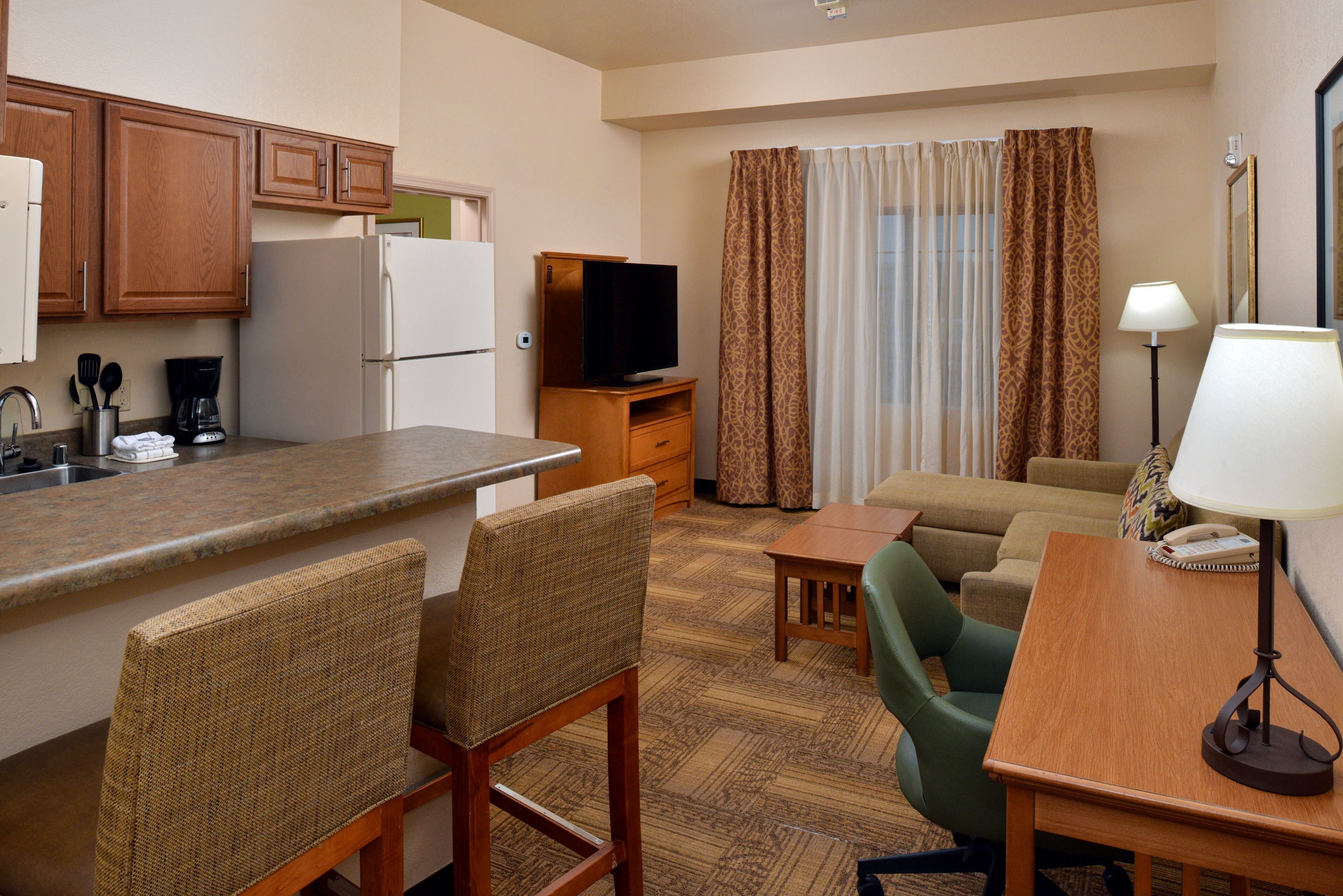 Quarto de hotel compacto com cozinha compacta, televisão de tela plana, sofá, mesa pequena e luminária.