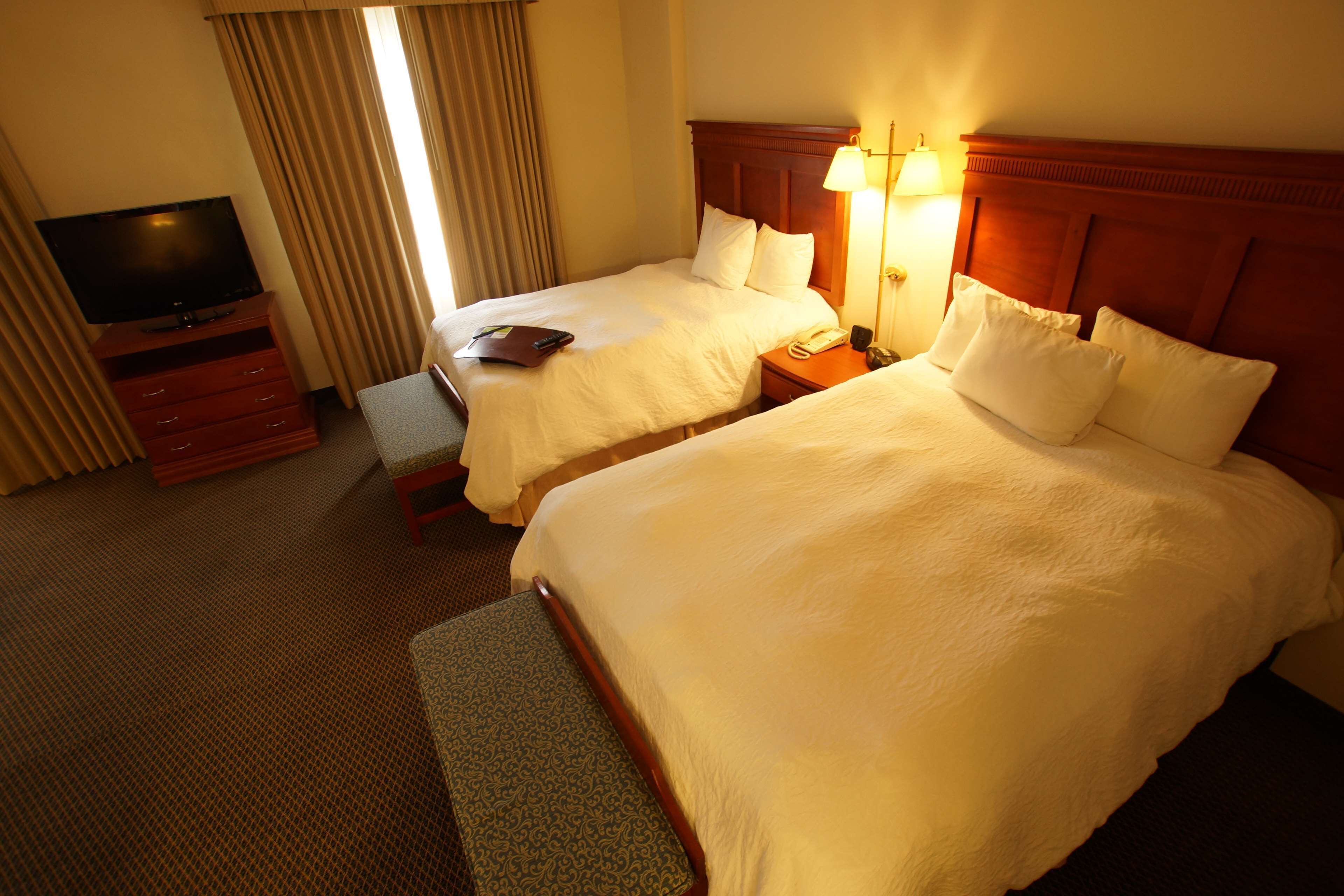 Quarto de hotel com duas camas, televisão, escrivaninha e abajur.