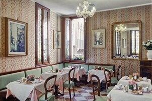 Uma sala de jantar com mesas preparadas para o café da manhã, com arranjos florais e um padrão de piso xadrez.