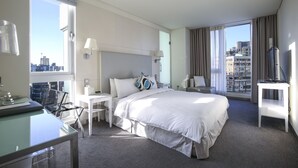 Quarto de hotel com uma cama grande, uma escrivaninha, uma cadeira, uma televisão e vista para a cidade.