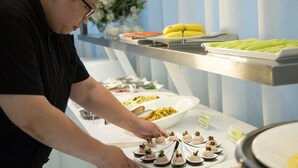 Disposição de buffet com diversos alimentos e uma pessoa servindo.