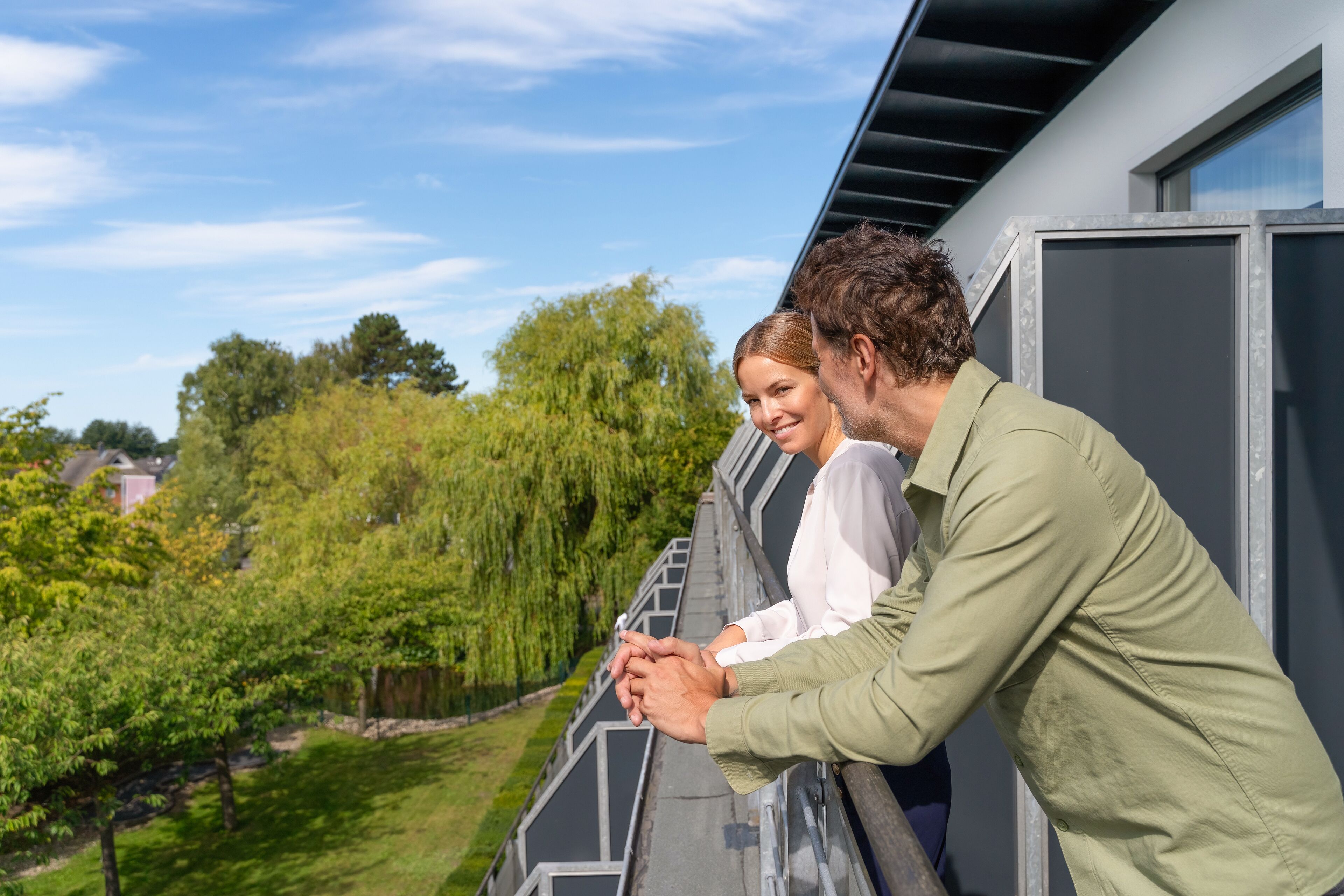 Um casal está em uma varanda com vista para um jardim e árvores.