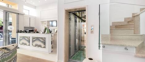 Um interior moderno com uma mesa de recepção, um elevador de vidro, uma escadaria e um vaso grande.