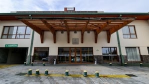 Entrada de hotel com galeria coberta, placa indicando estacionamento e céu claro.