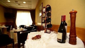 Uma área de refeições com uma mesa posta para dois, um suporte para vinhos e uma garrafa de vinho.