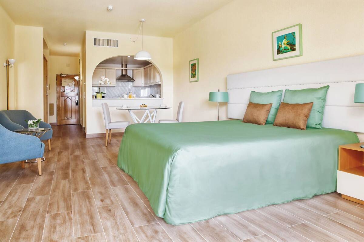 Quarto de hotel com cama, escrivaninha, cadeira, cozinha compacta e banheiro.