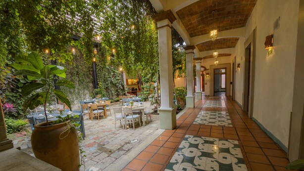 Pátio interno com piso de azulejos, mesas, cadeiras e plantas em vasos.