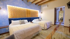Quarto de hotel com duas camas, cabeceira de madeira, parede azul e piso de madeira.