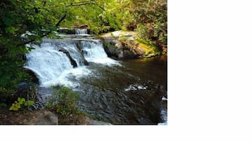 Uma cachoeira em área arborizada com terreno rochoso.