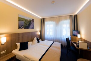Quarto de hotel com cama, escrivaninha com computador, televisão e quadro na parede.