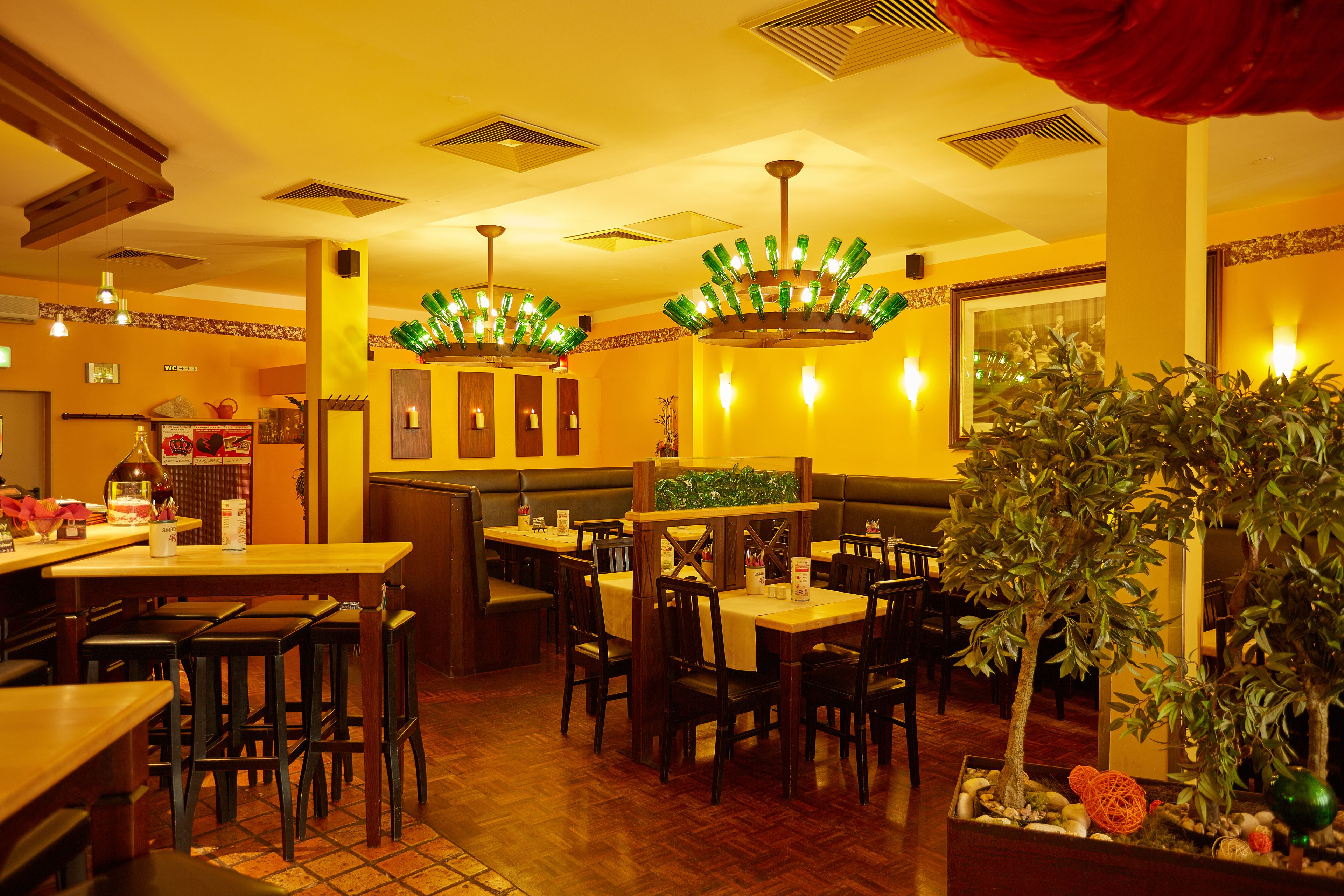 Um restaurante com mesas e cadeiras de madeira, um bar e uma grande planta em vaso.