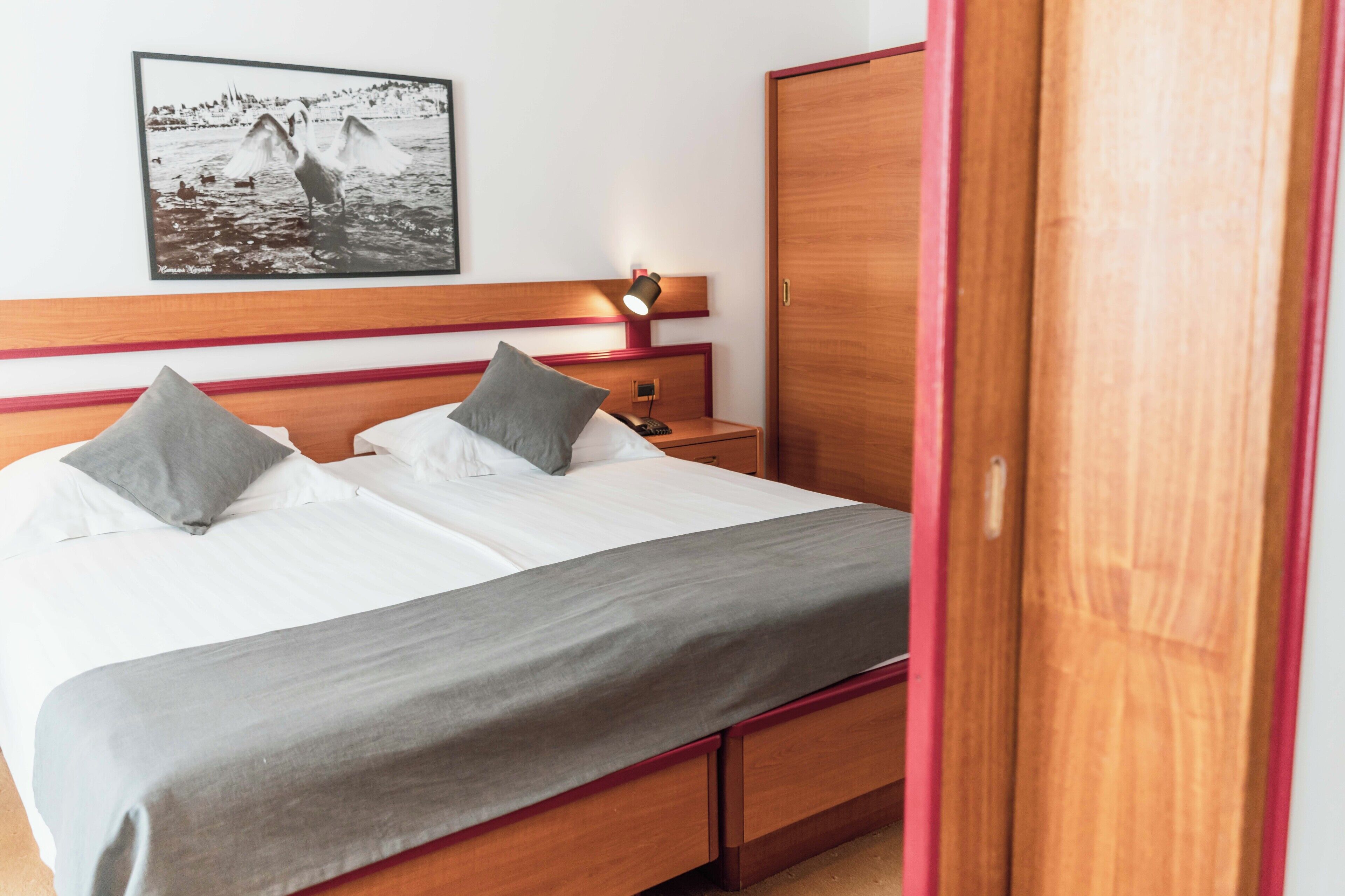 Uma cama bem arrumada com duas almofadas, uma mesa de cabeceira com abajur e um guarda-roupa de madeira.
