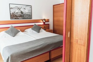 Uma cama bem arrumada com duas almofadas, uma mesa de cabeceira com abajur e um guarda-roupa de madeira.