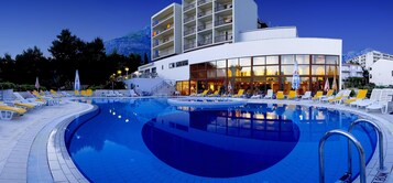 Um hotel com piscina, espreguiçadeiras e um edifício moderno com varandas.