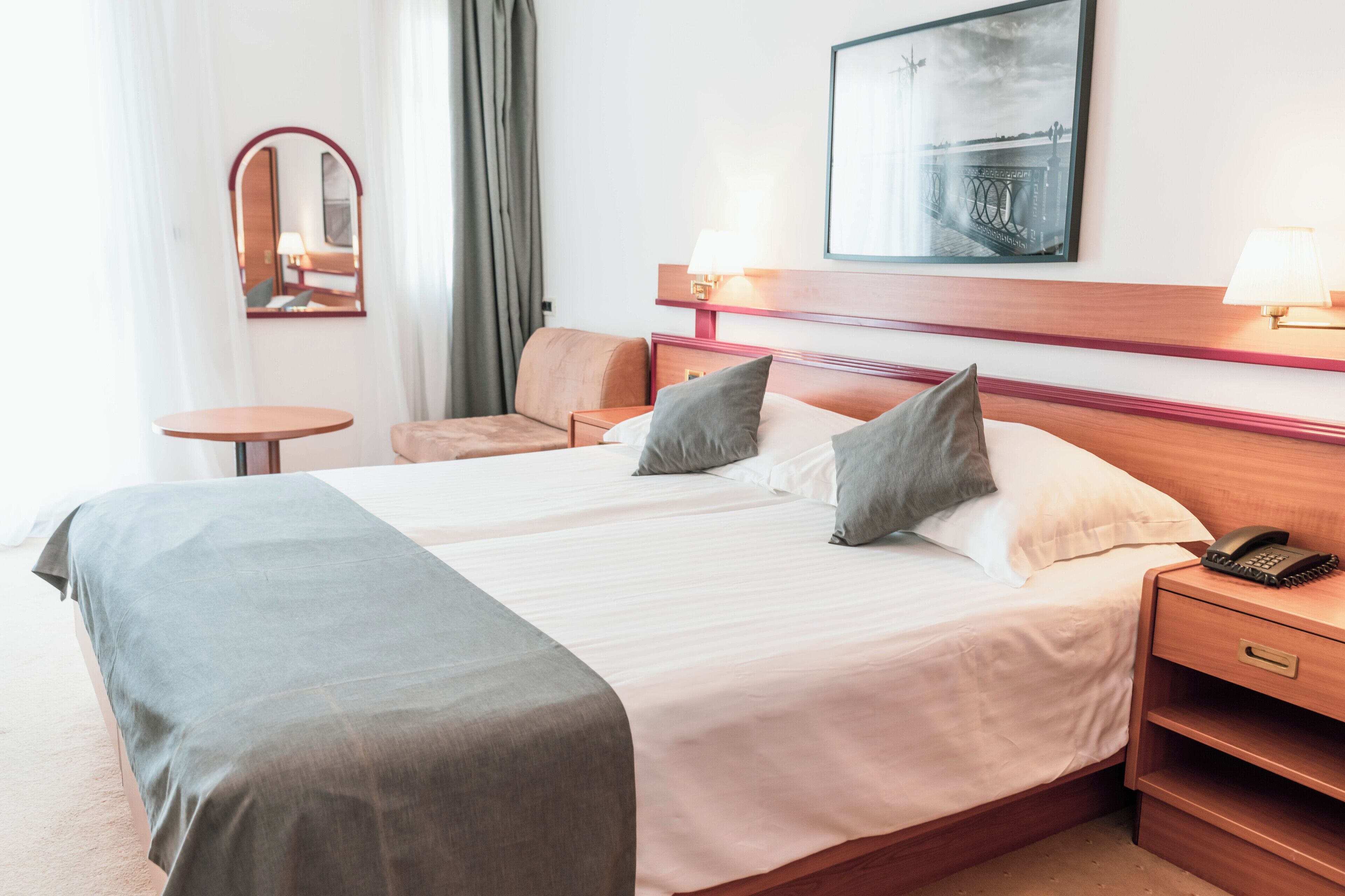 Quarto de hotel com uma cama grande, mesas de cabeceira, uma cadeira, um espelho e um quadro na parede.