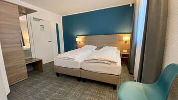 Quarto de hotel com cama de casal, escrivaninha, cadeira e parede azul.