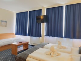 Quarto de hotel com cama, escrivaninha, TV de tela plana e janela com cortinas azuis.