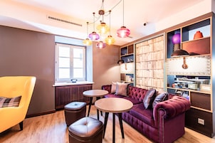 Um quarto aconchegante com um sofá vermelho macio, uma poltrona amarela, duas mesinhas redondas e uma estante repleta de livros e objetos decorativos.