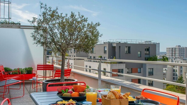 Espaço de refeições no terraço com mesa posta para o café da manhã, incluindo diversos pratos, bebidas e vista para a paisagem urbana.