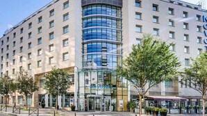 Um hotel moderno com fachada de vidro, entrada por porta giratória e restaurante visível chamado 