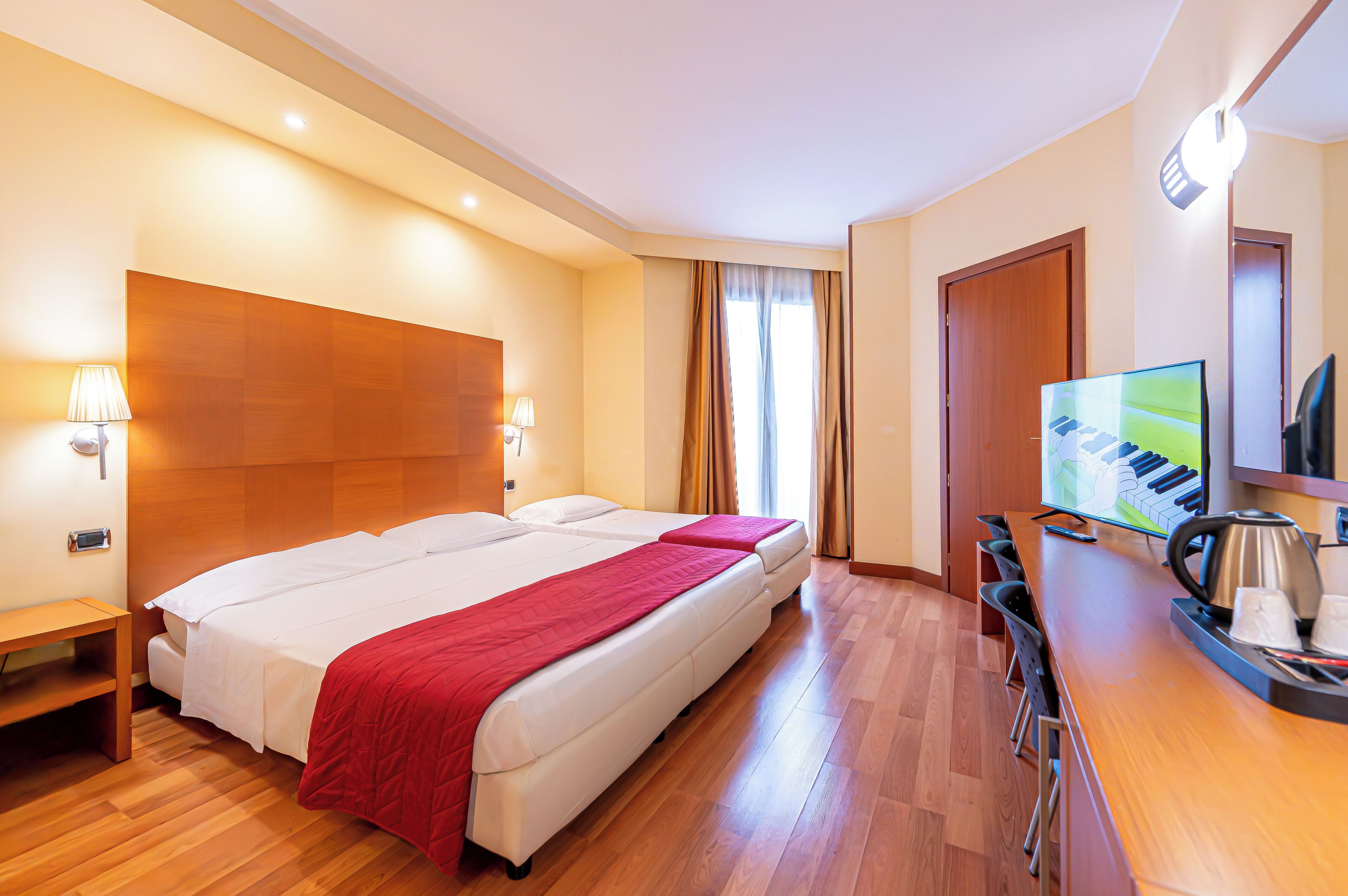 Quarto de hotel com cama, escrivaninha, televisão e máquina de café.