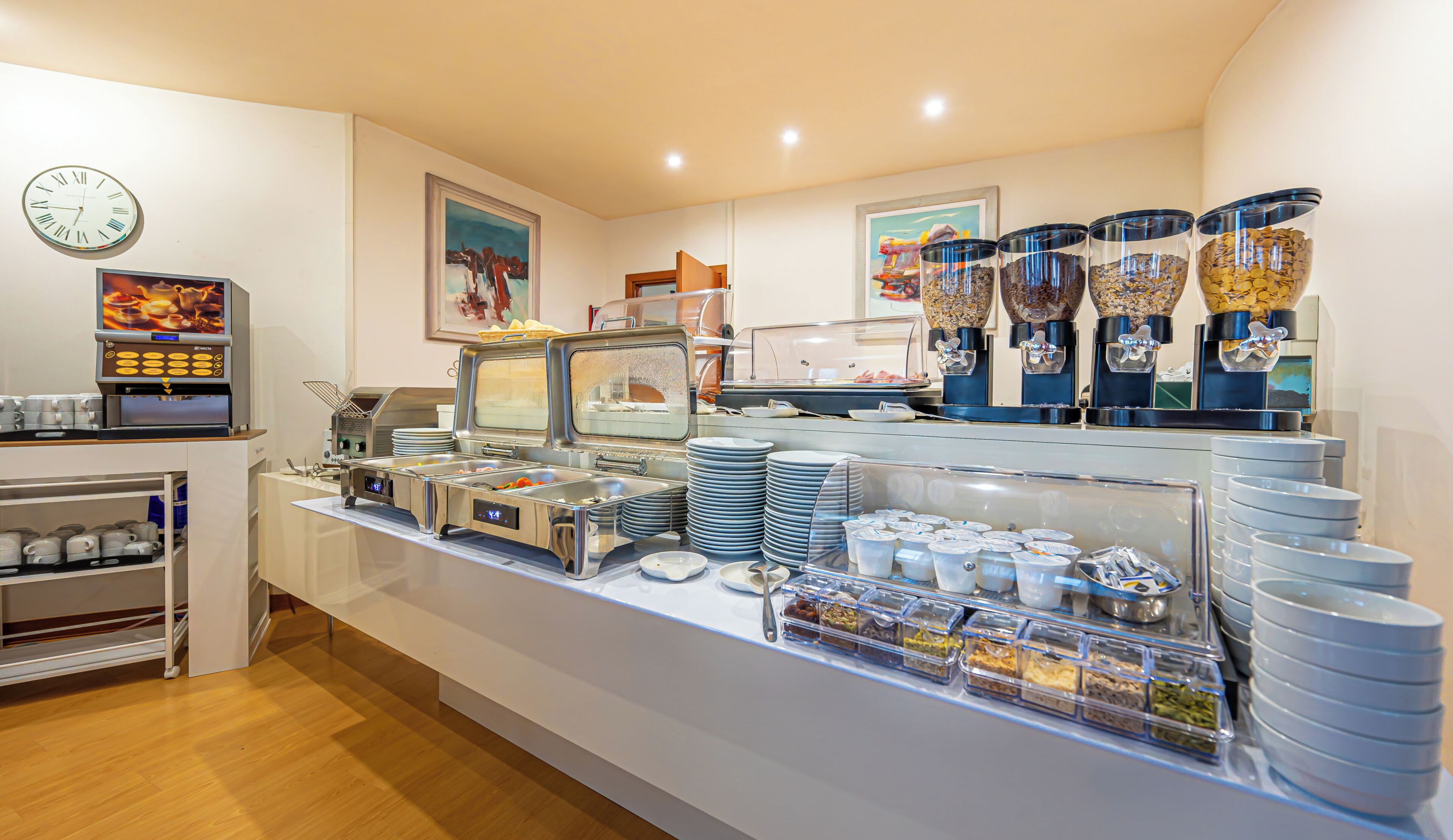 Uma mesa de buffet com máquina de café, distribuidores de alimentos e pilhas de pratos.